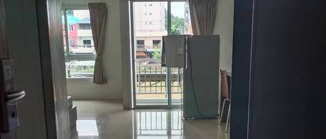 Corredor de hotel com piso de azulejos brilhantes, uma porta à esquerda e vista de um edifício através de uma porta de vidro.