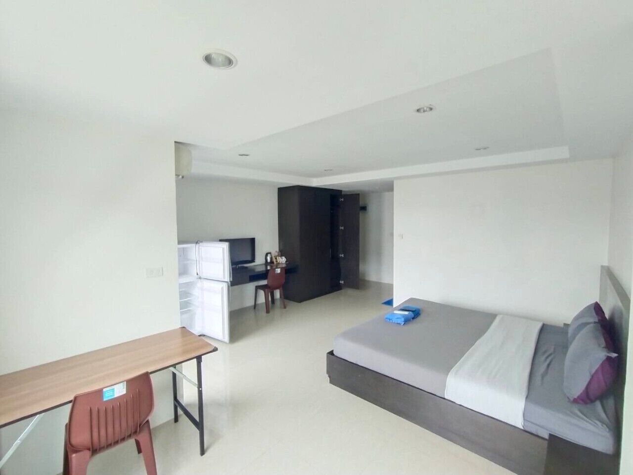 Quarto de hotel com cama, escrivaninha, cadeira, televisão e guarda-roupa.