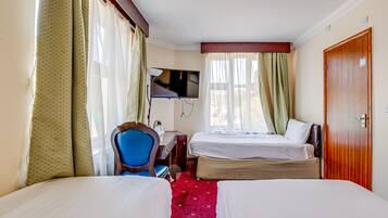 Quarto de hotel com duas camas, uma escrivaninha com cadeira, televisão e uma porta.