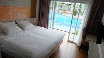 Quarto de hotel com uma cama grande, vista para uma piscina e porta de vidro corrediça para o exterior.