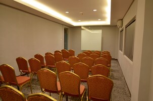 Uma sala de conferências com fileiras de cadeiras laranja e uma tela grande na frente.