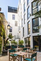 Um pátio com mesas ao ar livre, escadas e um edifício com várias janelas e varandas.