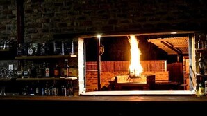 Uma área de bar com parede de tijolos, prateleiras com garrafas e uma lareira.