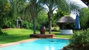 Piscina rodeada por vegetação exuberante, uma estrutura com telhado de palha e um gazebo branco.