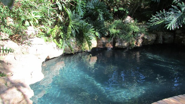 Piscina ao ar livre transparente, rodeada por formações rochosas naturais e vegetação.