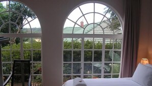 Quarto com cama, cadeira e grandes janelas com vista para o verde.