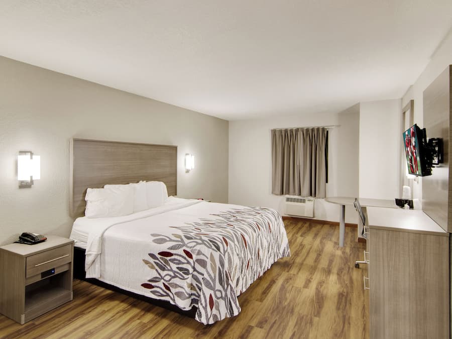 Quarto de hotel com cama, mesa de cabeceira, luminária e espelho.
