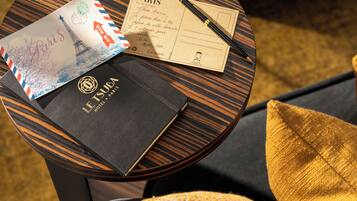 Uma mesa redonda de madeira com um caderno preto, um postal, uma caneta e um pequeno envelope.
