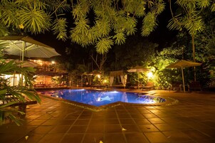 Uma área de piscina à noite, com chão ladrilhado, guarda-sóis e mobiliário de exterior.