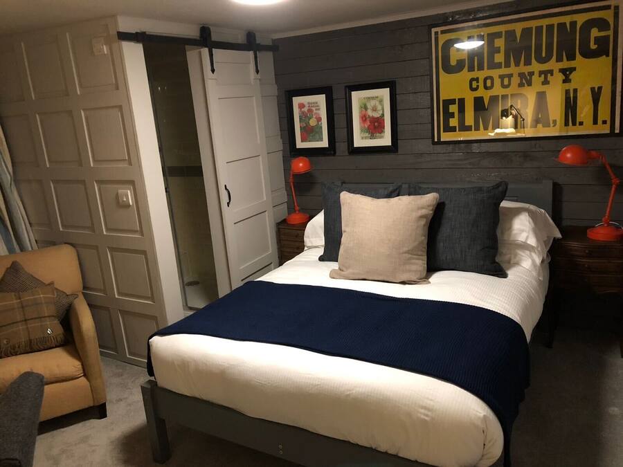 Quarto com cama, duas mesas de cabeceira, uma cadeira, guarda-roupa e parede com um letreiro emoldurado.
