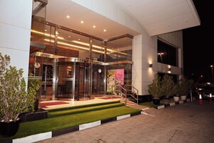 Entrada moderna de hotel com porta giratória, fachada de vidro e tapete vermelho até a entrada.