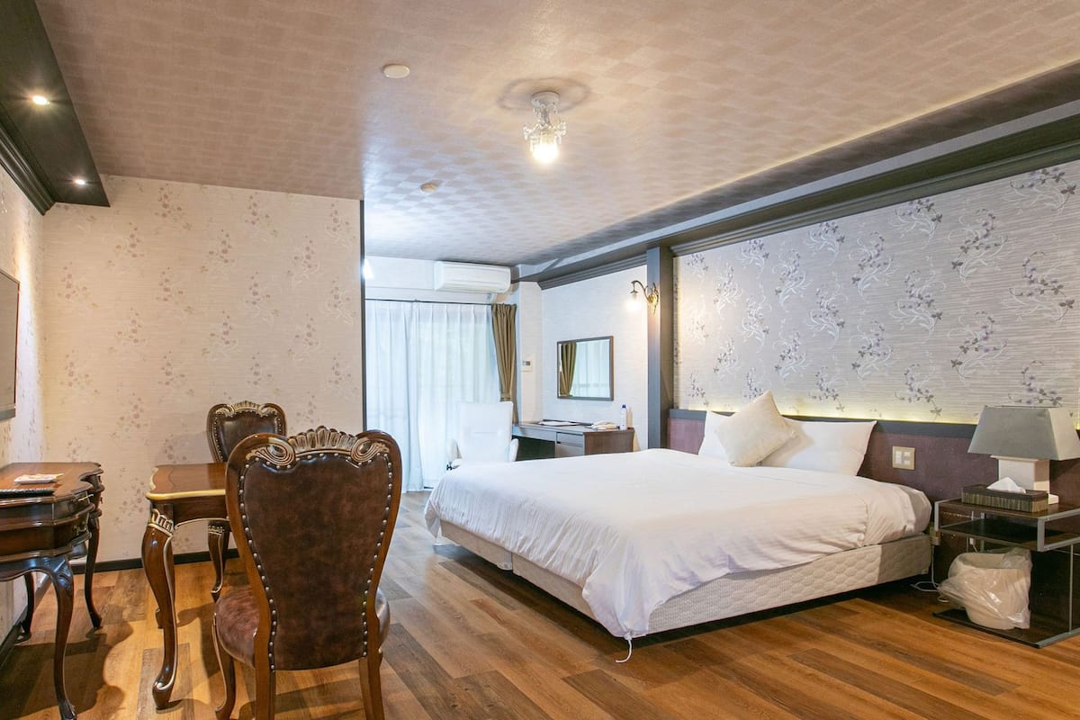 Quarto de hotel com cama, escrivaninha, cadeira, televisão e janela com cortinas.