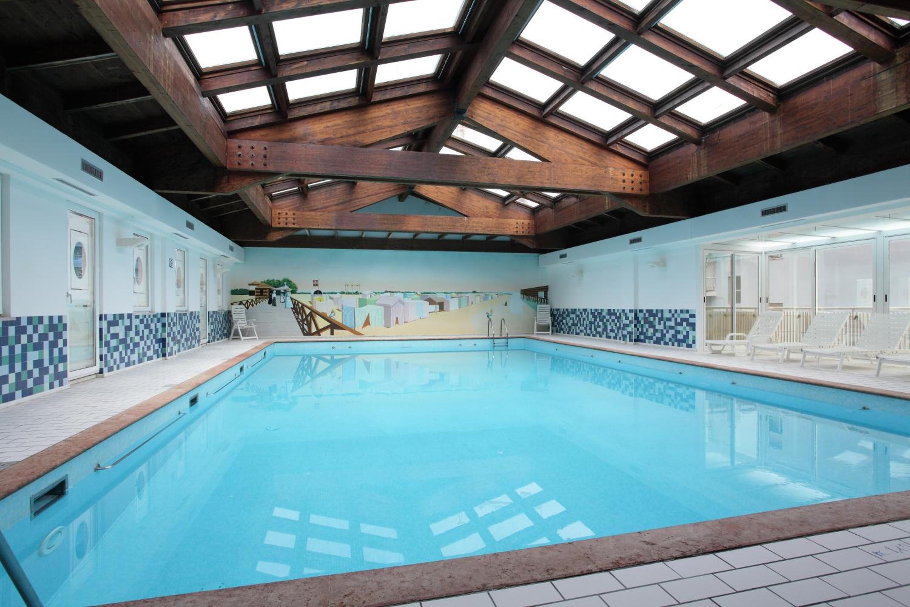 Piscina interna com teto skylight, paredes azulejadas e cadeiras de lounge.