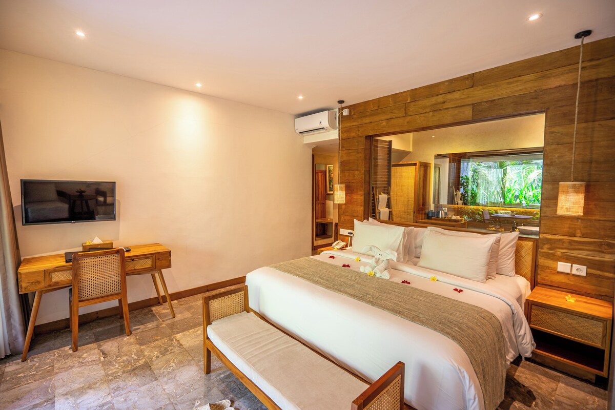 Quarto de hotel com cama, escrivaninha, cadeira e televisão.
