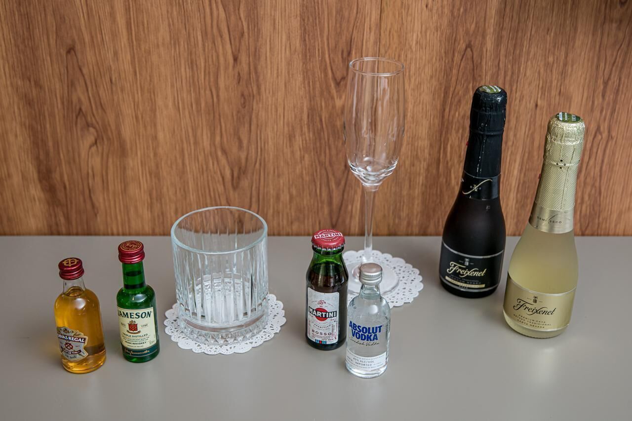 Uma mesa com diversas garrafas de bebidas alcoólicas e um copo de vidro transparente.