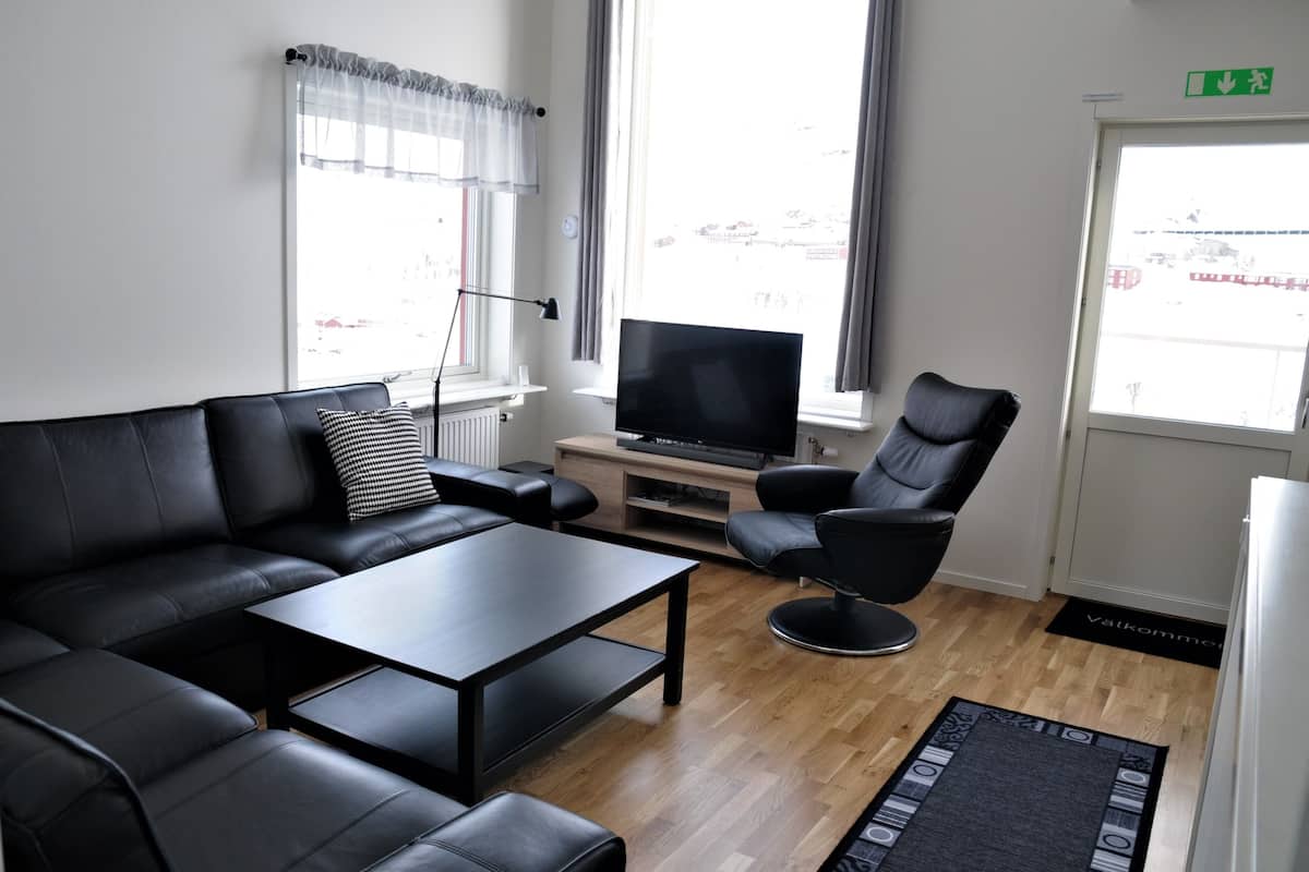 Uma sala de estar moderna com um sofá de couro preto, uma poltrona preta, uma mesa de centro de madeira e uma TV de tela plana sobre um suporte de madeira.