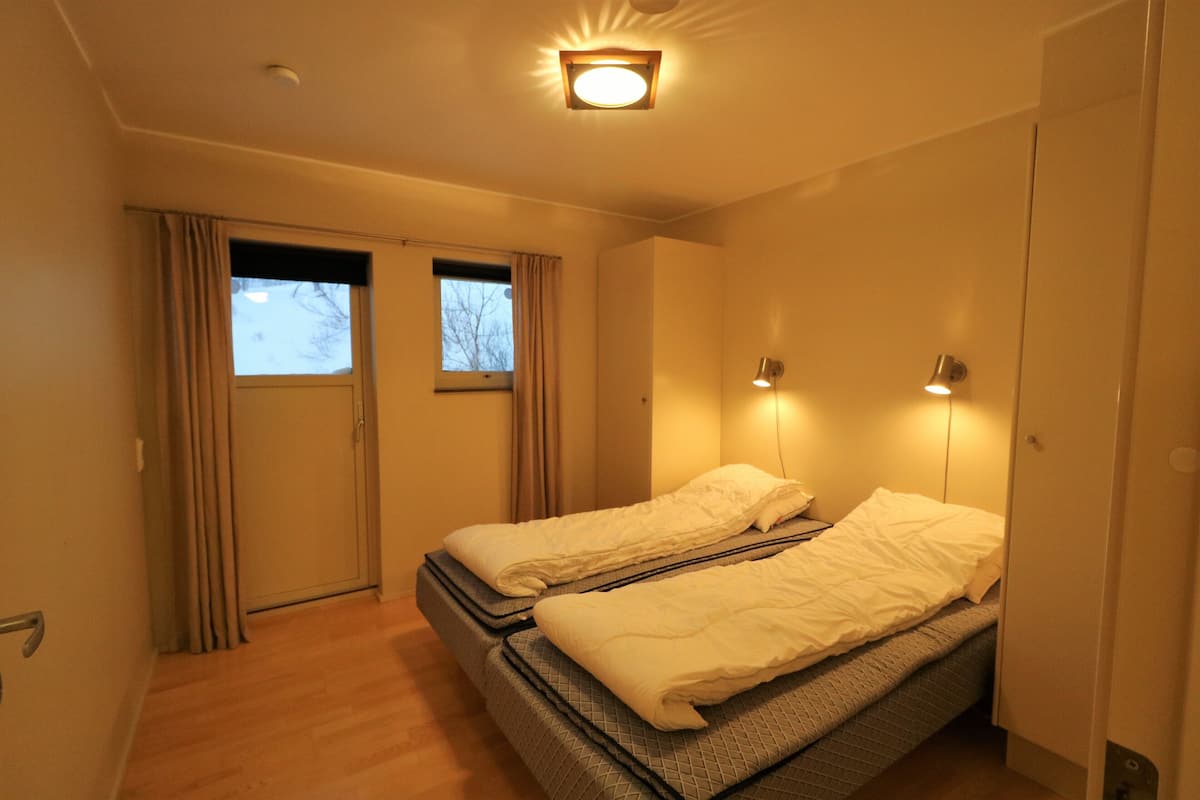 Quarto com duas camas, uma janela com cortinas e luminária no teto.