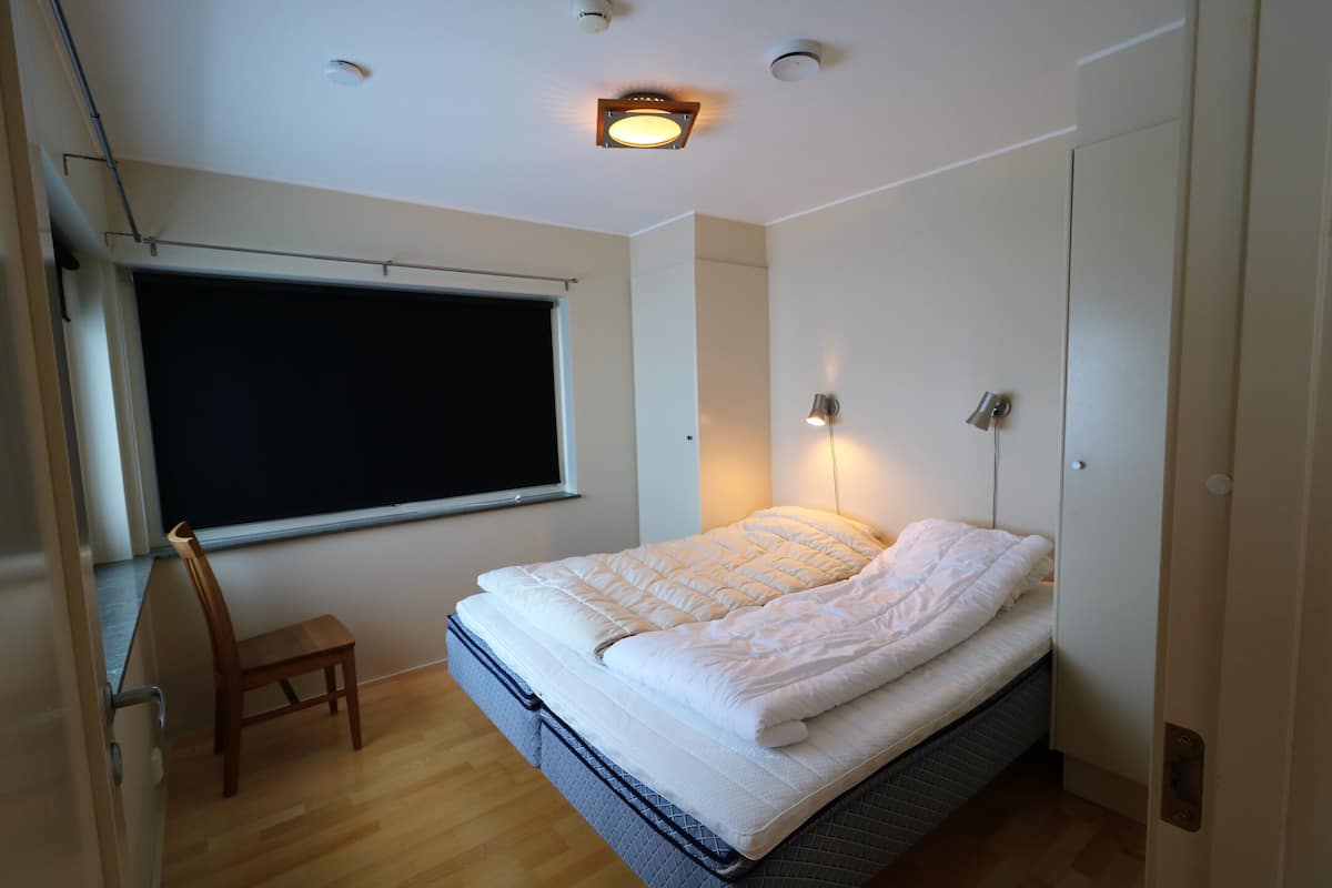 Quarto com cama, cadeira, janela e luminária fixada na parede.