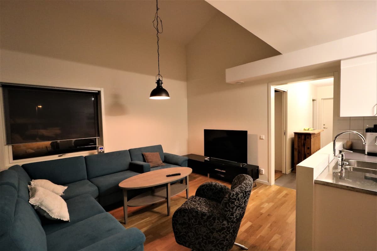 Uma sala de estar moderna com sofá, televisão e uma pequena mesa.