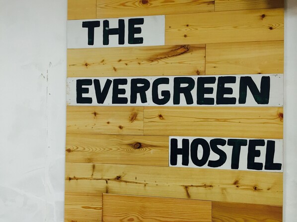 Uma placa com o texto 'THE EVERGREEN HOSTEL' em uma parede de madeira.