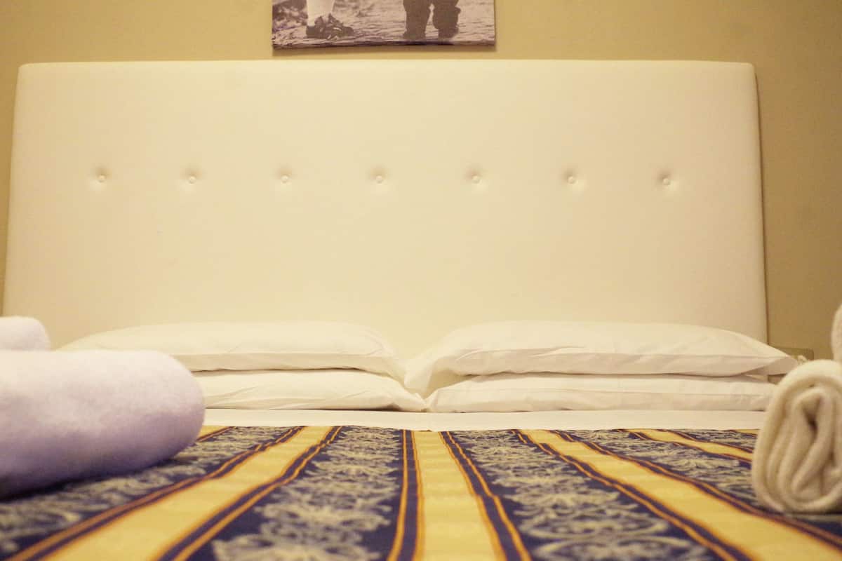 Cama bem arrumada com lençóis brancos e colcha estampada.
