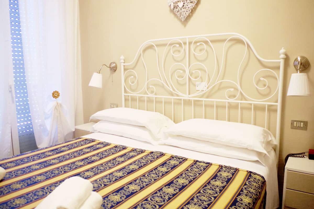 Uma cama com cabeceira branca, colcha estampada e duas luminárias de mesa.
