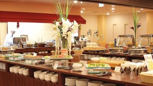 Buffet montado com diversas estações de comida, um chef ao fundo e um arranjo floral decorativo.