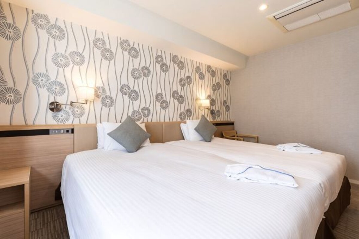 Quarto de hotel com cama grande, duas mesas de cabeceira, ar condicionado fixado na parede e painel decorativo.