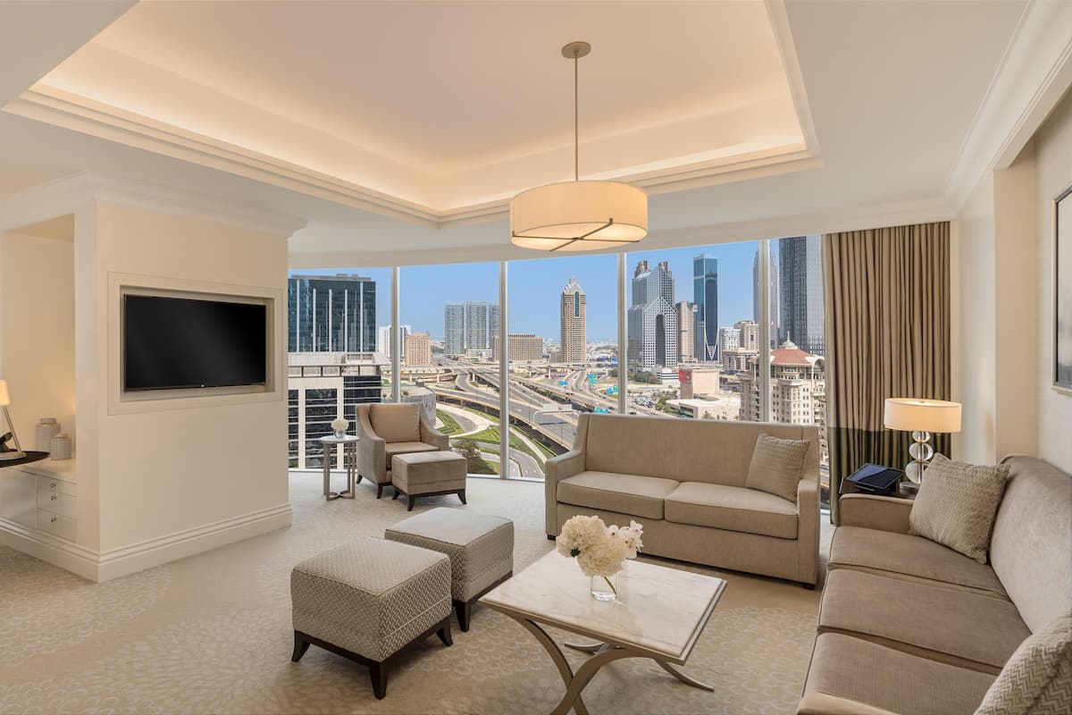 Quarto de hotel espaçoso com ampla vista da cidade, televisão de tela plana na parede, sofá confortável, escrivaninha com cadeira e mesa de centro.