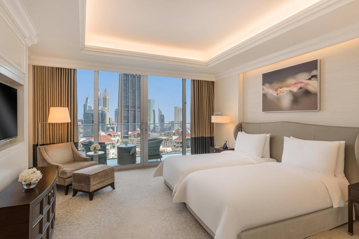 Quarto de hotel com duas camas, televisão, secretária e vista para o horizonte da cidade.