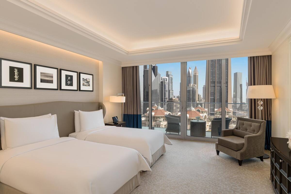 Quarto de hotel com duas camas, televisão, escrivaninha e vista para a cidade.