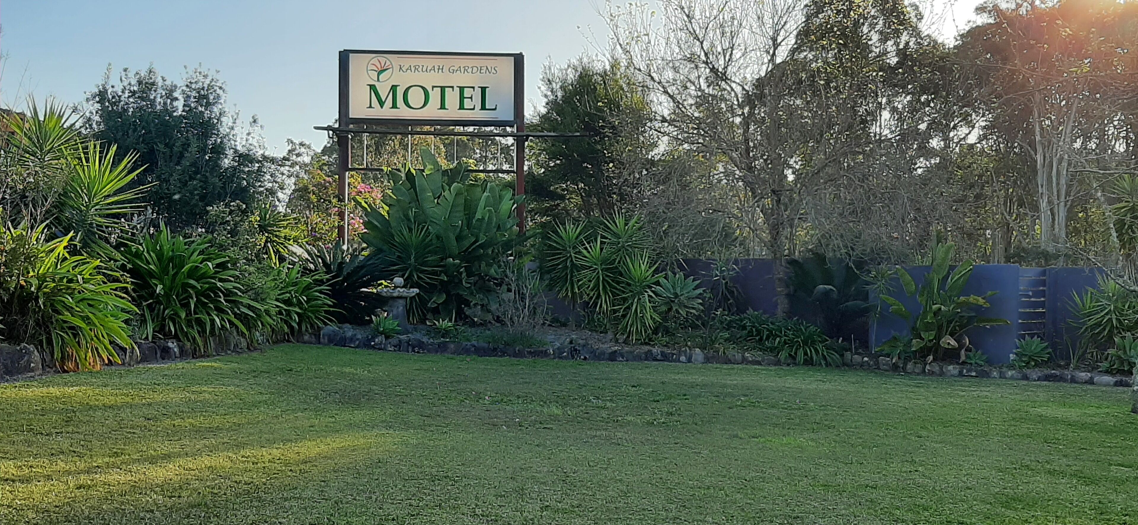 Placa do Karuah Gardens Motel, rodeada por vegetação exuberante e um gramado bem cuidado.