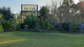 Placa do Karuah Gardens Motel, rodeada por vegetação exuberante e um gramado bem cuidado.