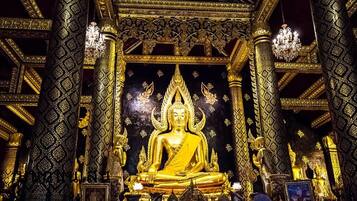 Uma estátua dourada de Buda em um templo com padrões de ouro elaborados e lustres.