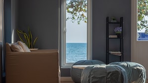 Quarto com sofá, poltronas de saco, estante de livros e vista para o mar.