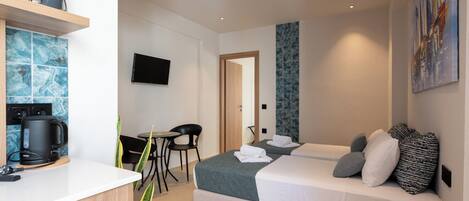 Quarto de hotel com cozinha compacta, uma cama, escrivaninha e uma cadeira.