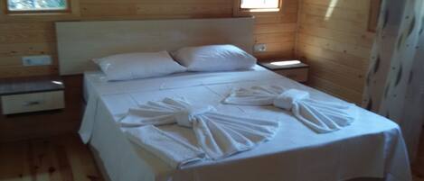 Quarto de cabana de madeira com cama, travesseiros, mesa de cabeceira e gaveta.