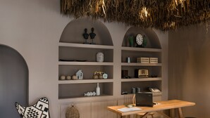 Quarto moderno com uma escrivaninha de madeira, um laptop e uma cadeira. Estantes com objetos decorativos e um relógio são visíveis.