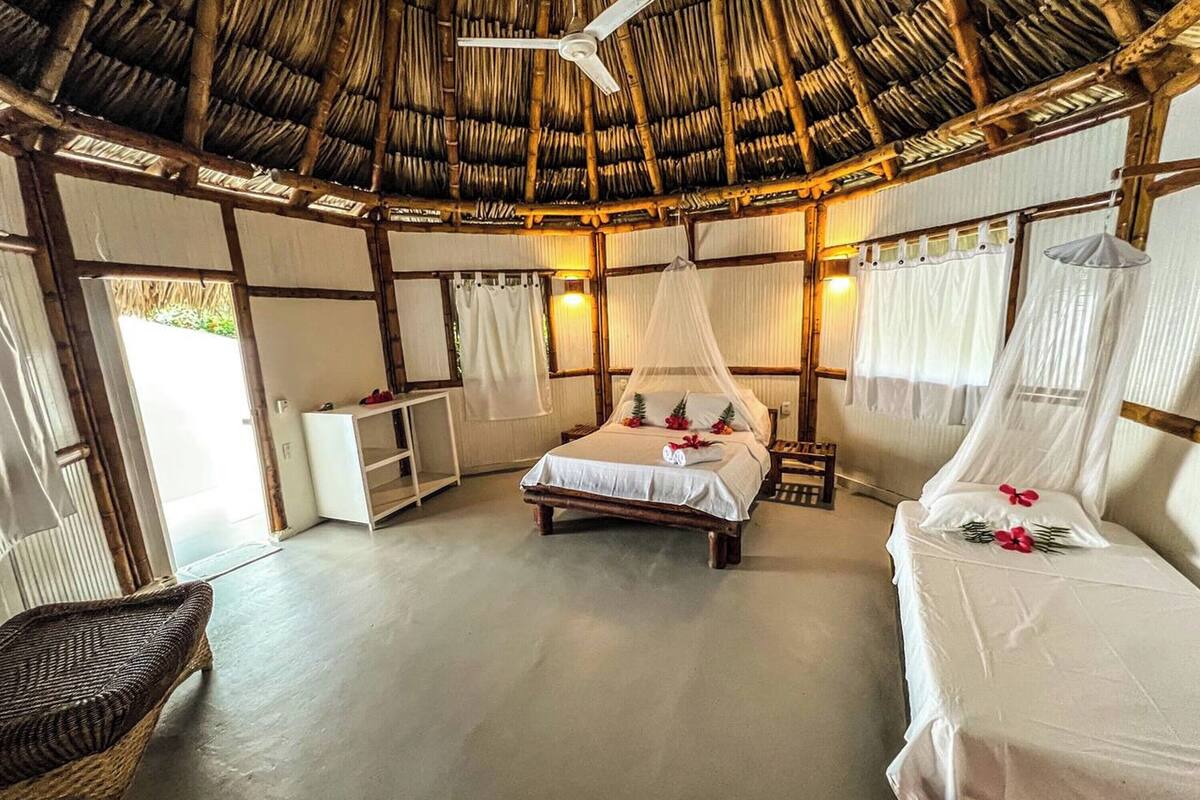 Um quarto com telhado de palha, uma cama com dossel, uma mesinha de cabeceira e uma cadeira.