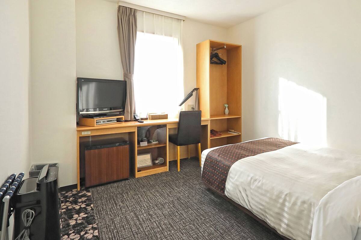 Quarto de hotel com cama, secretária com televisão, cadeira, guarda-roupa e chão coberto de carpete.