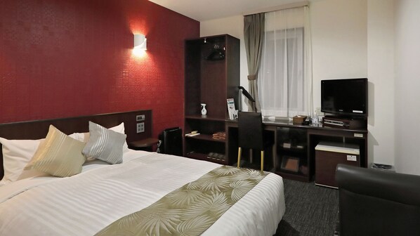 Quarto de hotel com uma cama grande, escrivaninha com computador, televisão e minibar.