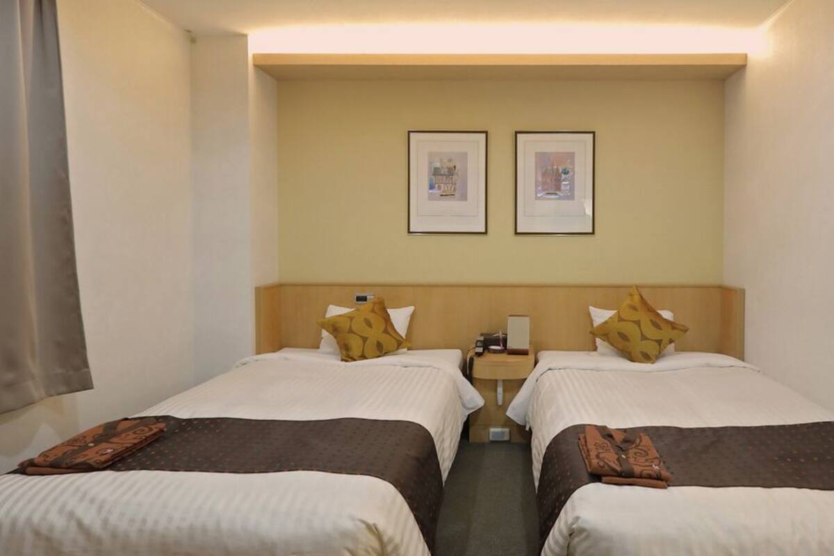 Quarto de hotel com duas camas, uma mesa de cabeceira, uma luminária e duas fotos emolduradas na parede.