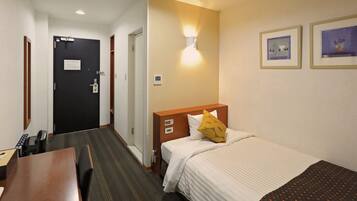 Quarto de hotel com cama, escrivaninha, cadeira, luminária na parede e duas imagens emolduradas.