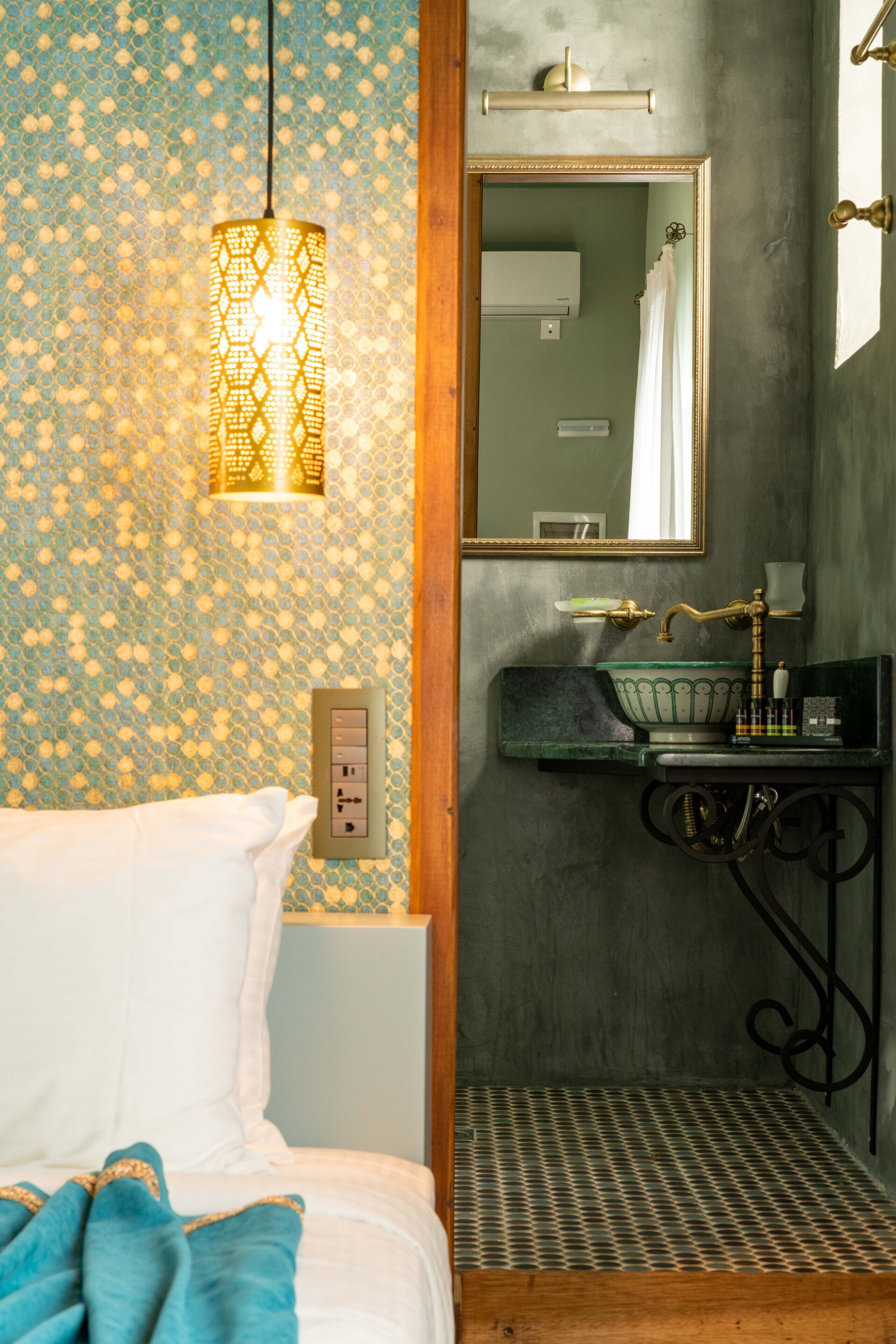 Casa de banho com parede estampada, candeeiro pendente, lavatório com cuba verde e espelho em cima.
