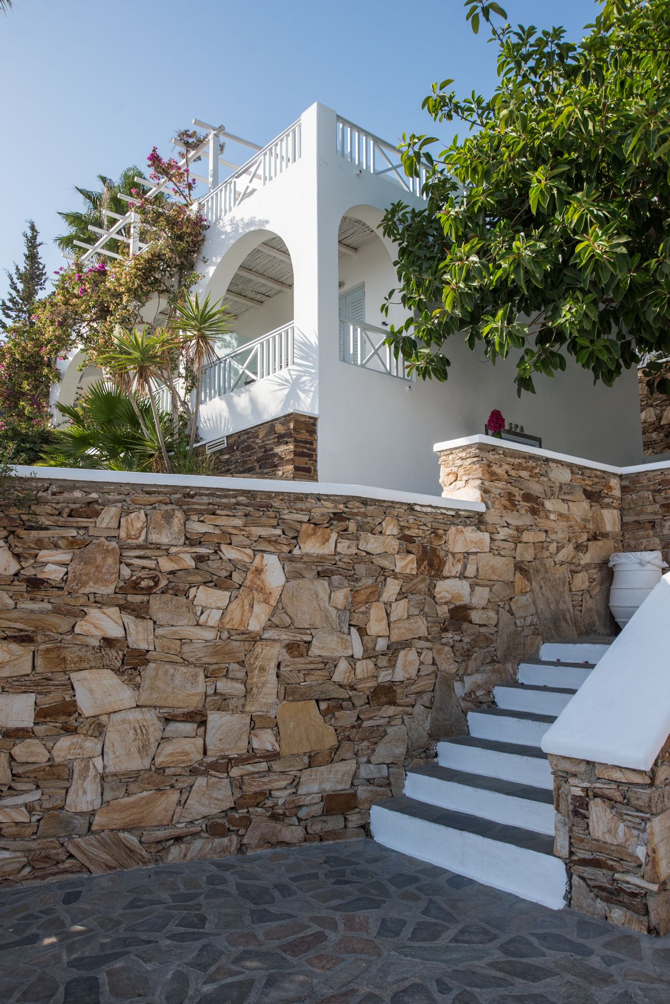 Uma escadaria de pedra leva a um edifício branco com arcos e varanda.