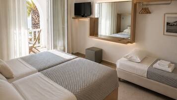 Quarto de hotel com cama, sofá, televisão, espelho e janela com cortinas.