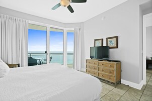 Quarto de hotel com uma cama grande, televisão sobre uma cômoda de madeira e varanda com vista para o oceano.