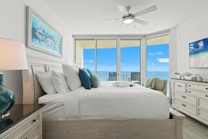 Quarto com cama, ventoinha no teto, mesa de cabeceira, cômoda e vista para o oceano.