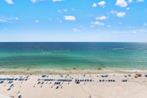 Uma praia com águas cristalinas azuis, areal arenoso e vários guarda-sóis.