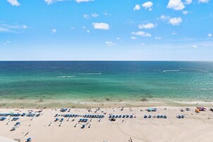 Uma praia com águas cristalinas azuis, areal arenoso e vários guarda-sóis.